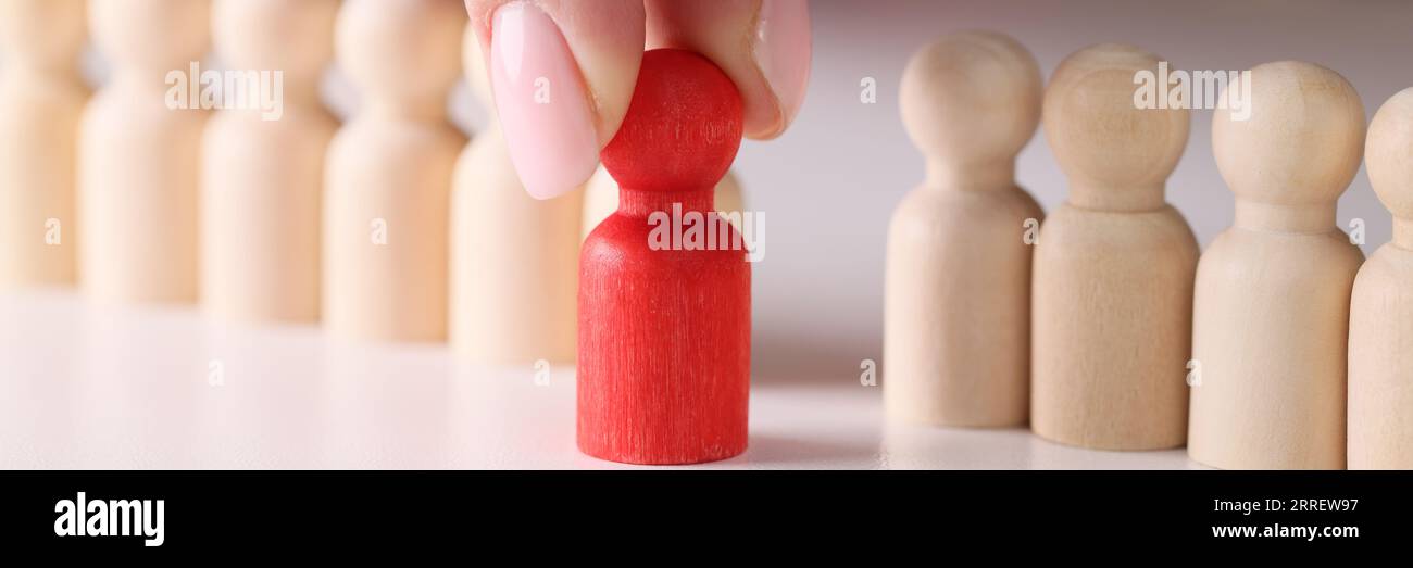 Human hand takes one red figure from group of many ordinary wooden ...