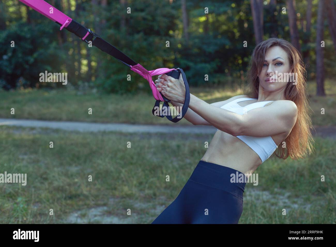 A woman is engaged in a sports rubber simulator stretching an elastic ...