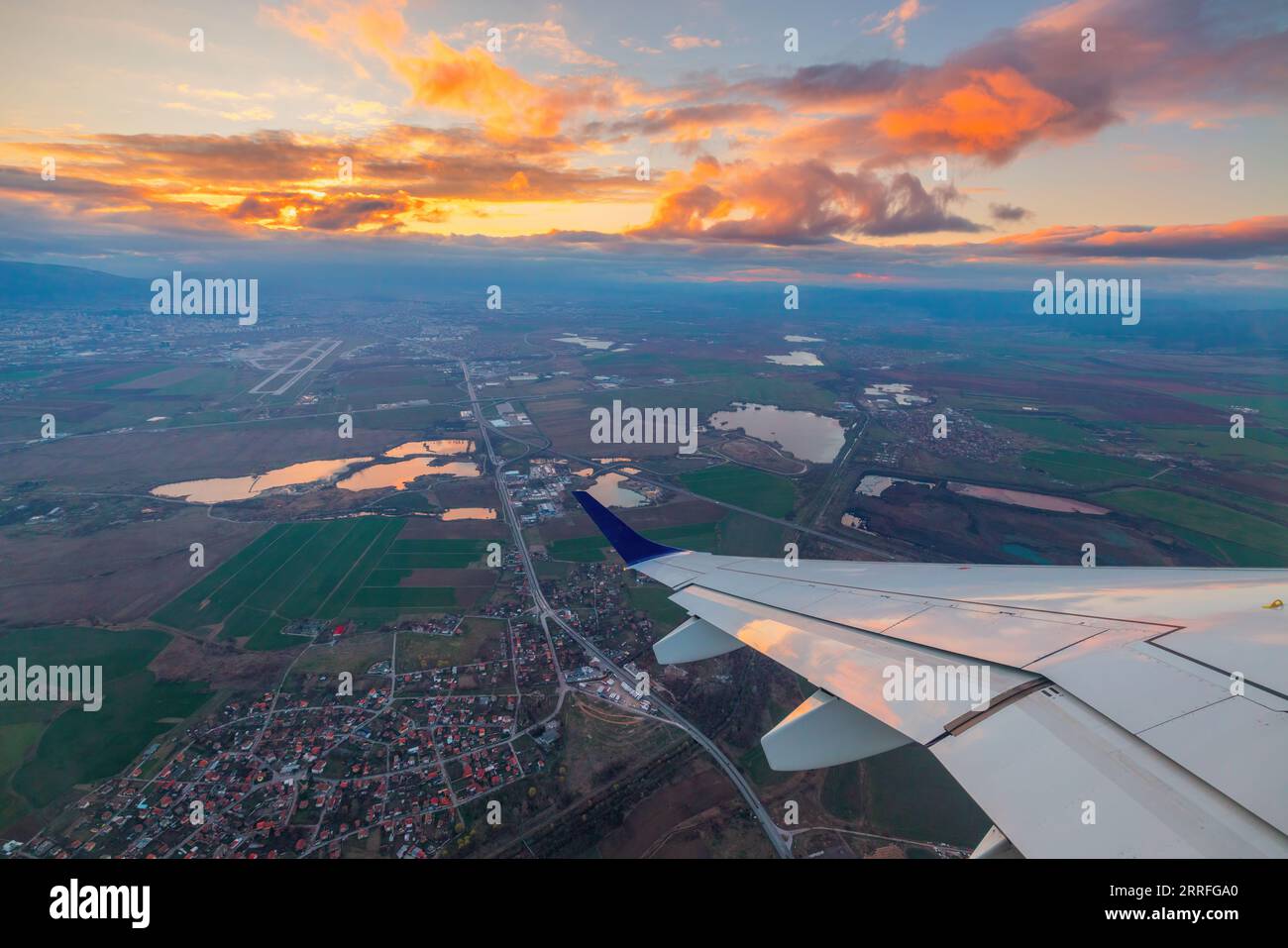 Airplane flight in sunset sky over city and wing of plane. View from ...