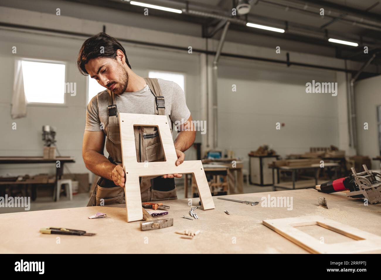 Young man carpenter wearing uniform working in joinery making wooden ...
