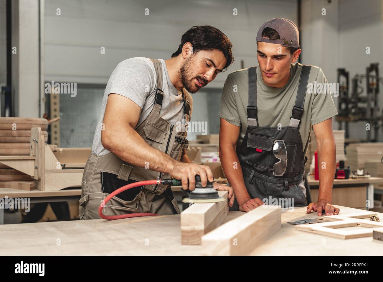 Two young carpenters working with wood standing at table in workshop ...