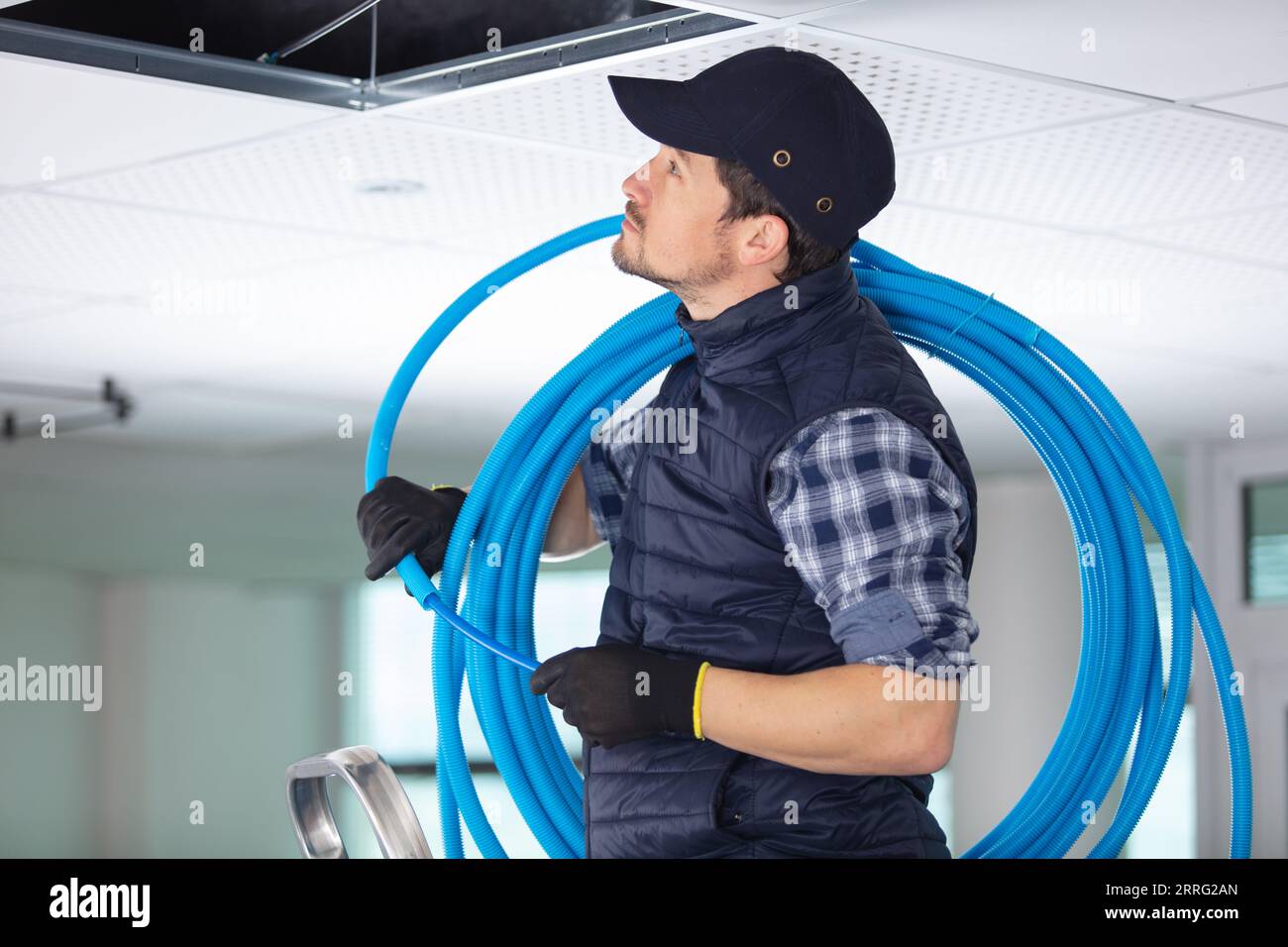 male tradesman with reel of blue pipe on his shoulder Stock Photo - Alamy