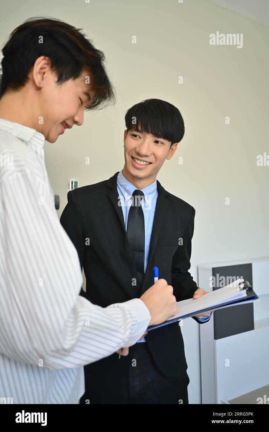 Happy young asian man signing contract with realtor. First property ...