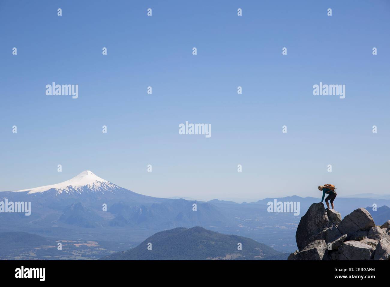 Hiker climbs boulder with snow capped volcano behind Stock Photo - Alamy