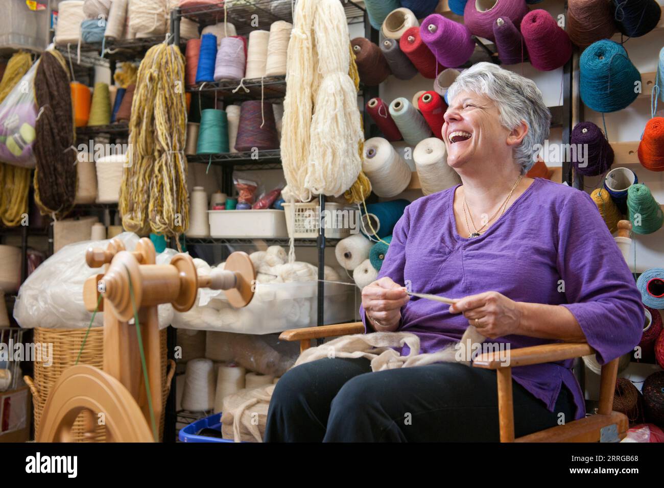Senior woman laughs while handspinning wool into yarn at a fiber arts ...
