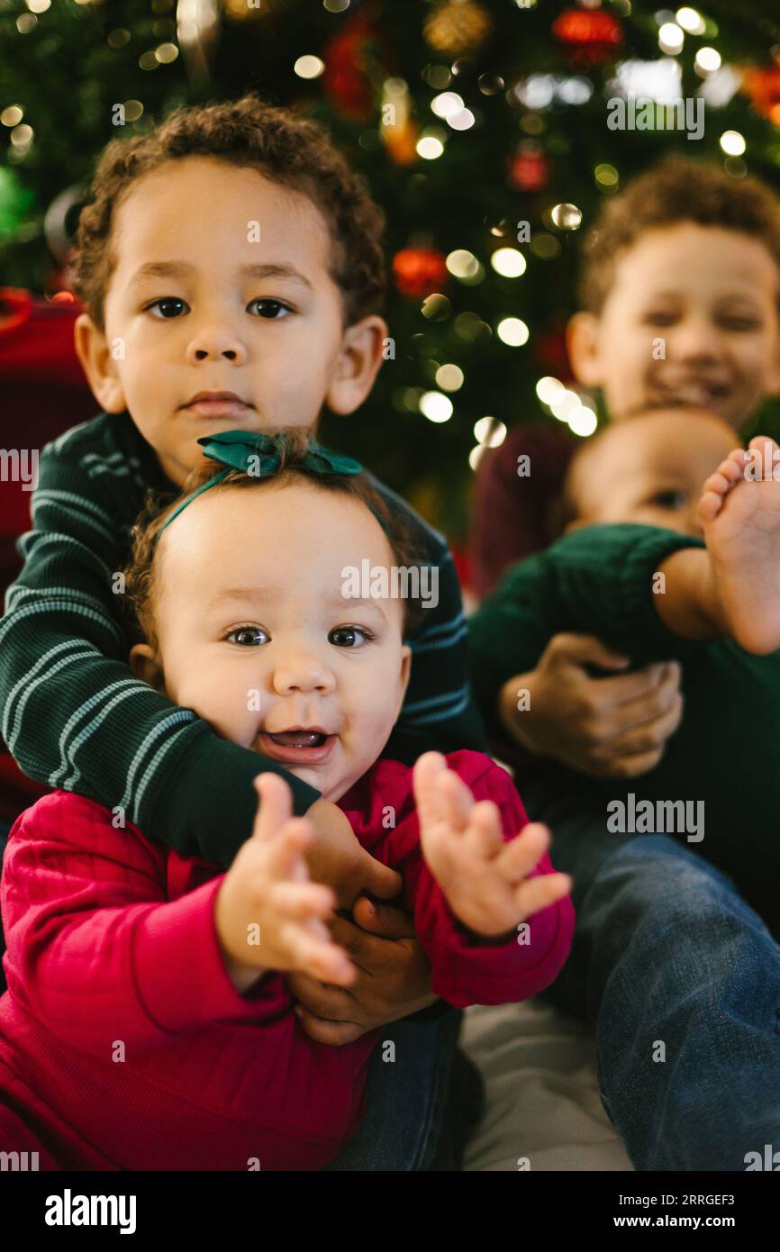 Toddler boy holds baby sister as they smile with siblings at christmas ...