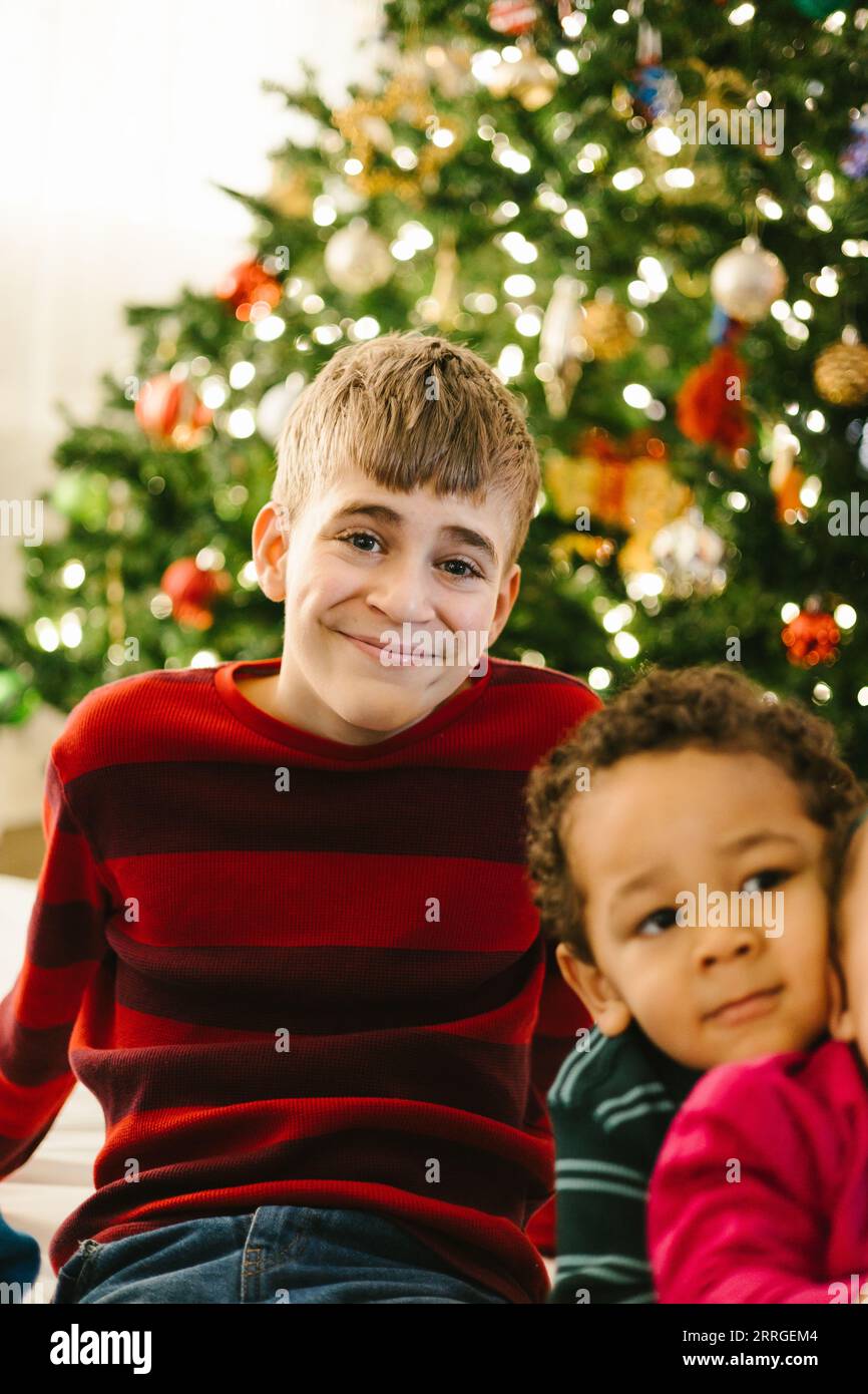 Smiling happy tween with siblings at christmas with lights and trees ...