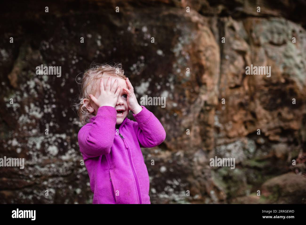Little girl playing peek-a-boo on a hike in front of a rock wall Stock ...