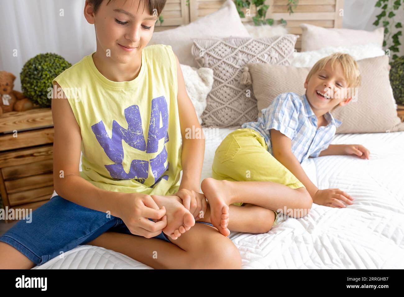 Happy positive children, tickling on the feet, having fun together, boy brothers at home having ...