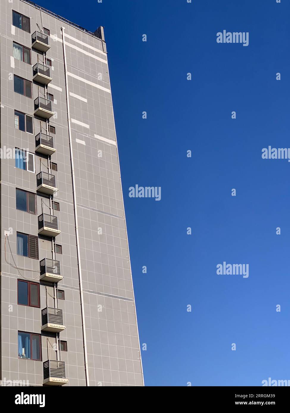 A tall gray high-rise building featuring balconies on its upper floors ...
