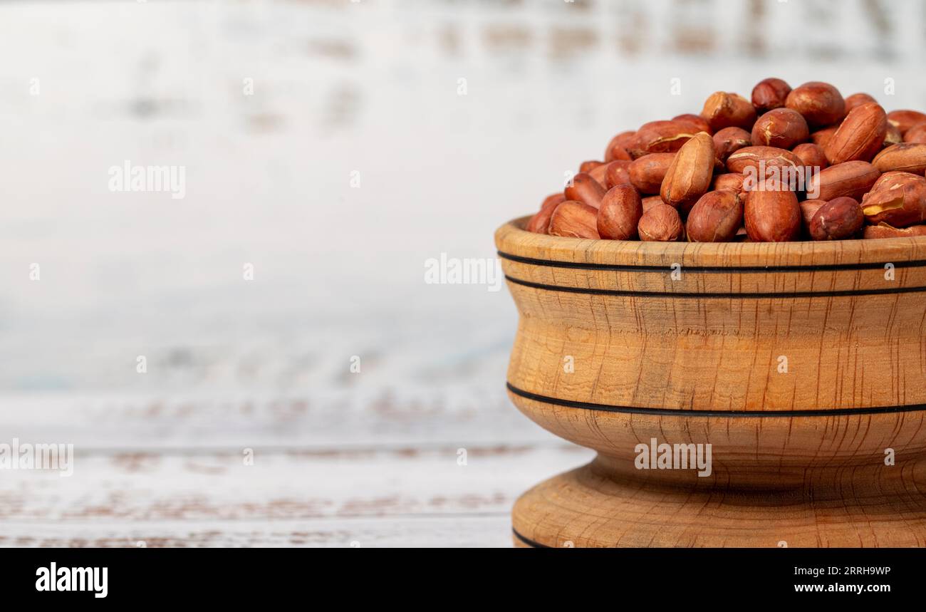 Peanuts in wooden bowl. Peanuts in shell on white wood background. Copy space. Empty space for ...