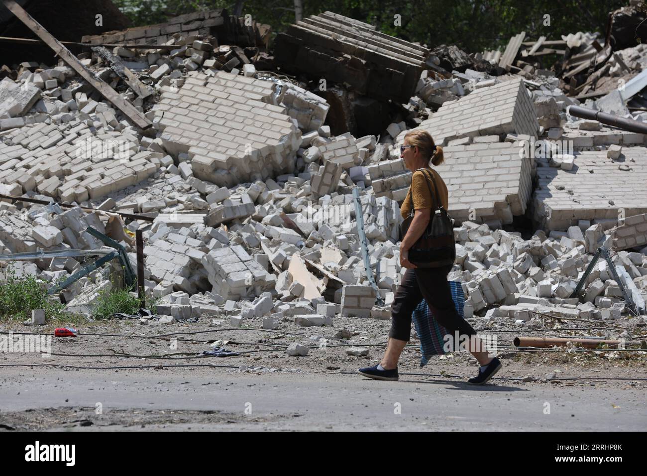220706 -- LYSYCHANSK, July 6, 2022 -- A resident passes by destroyed ...
