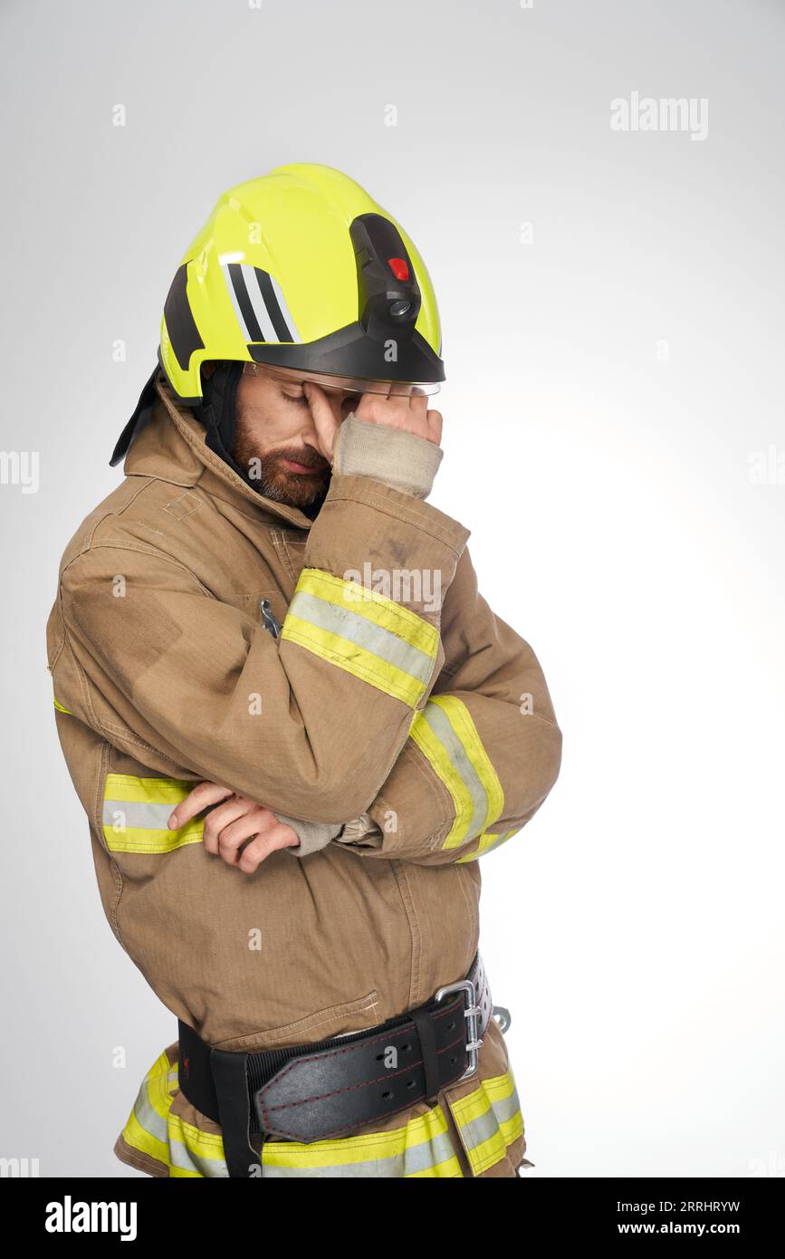 Sad, exhausted firefighter in uniform tiredly rubbing forehead in ...
