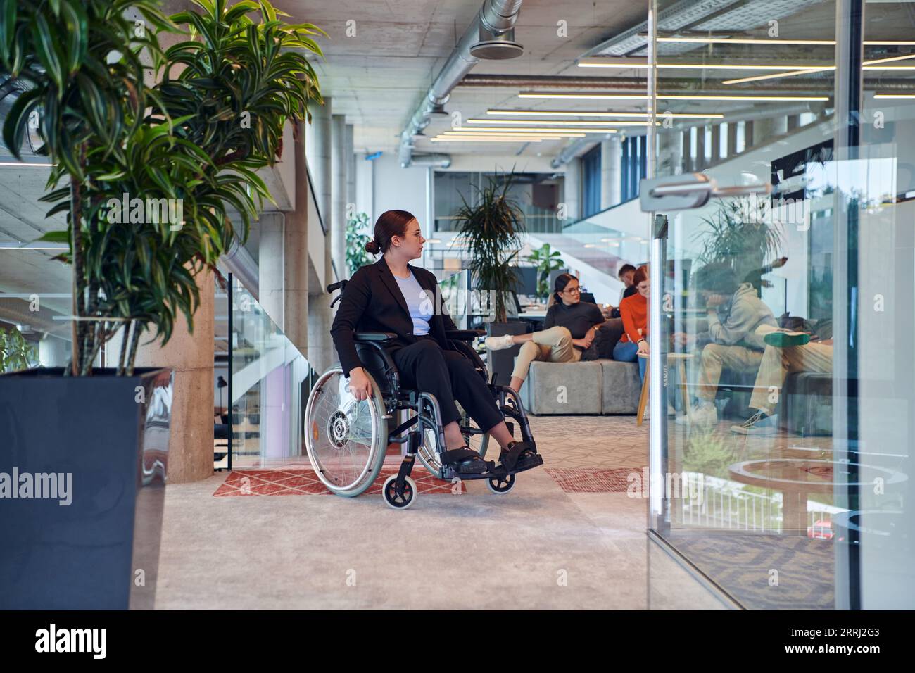 In a modern office, a young businesswoman in a wheelchair is surrounded ...