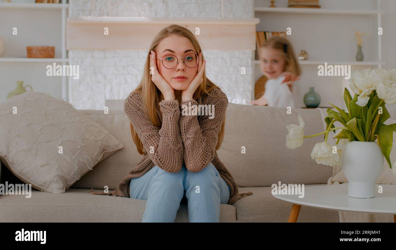 Tired upset Caucasian mother sitting on sofa at home sad frustrated ...