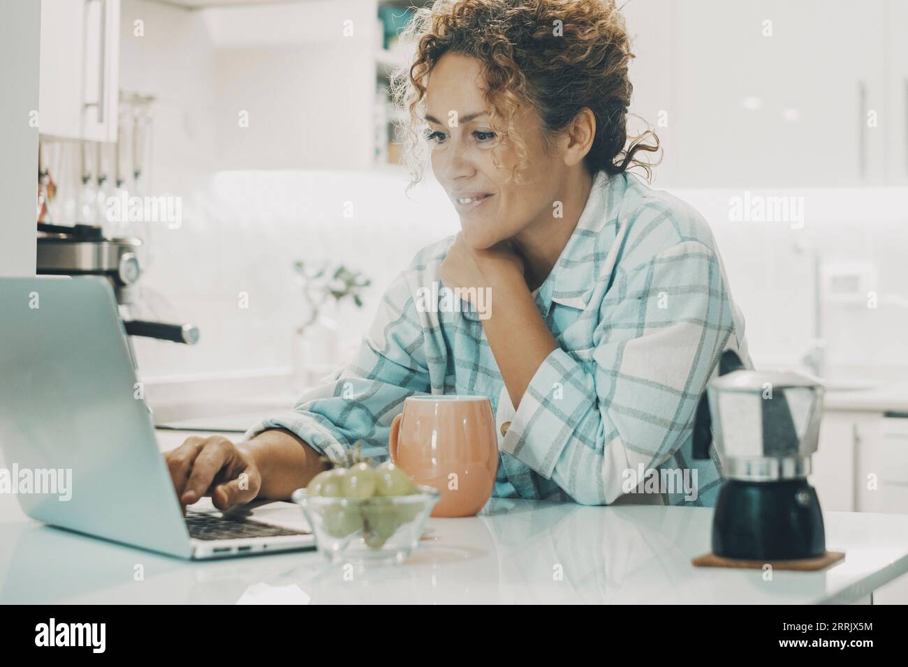 Portrait of happy woman smiling in front of a laptop writing and ...