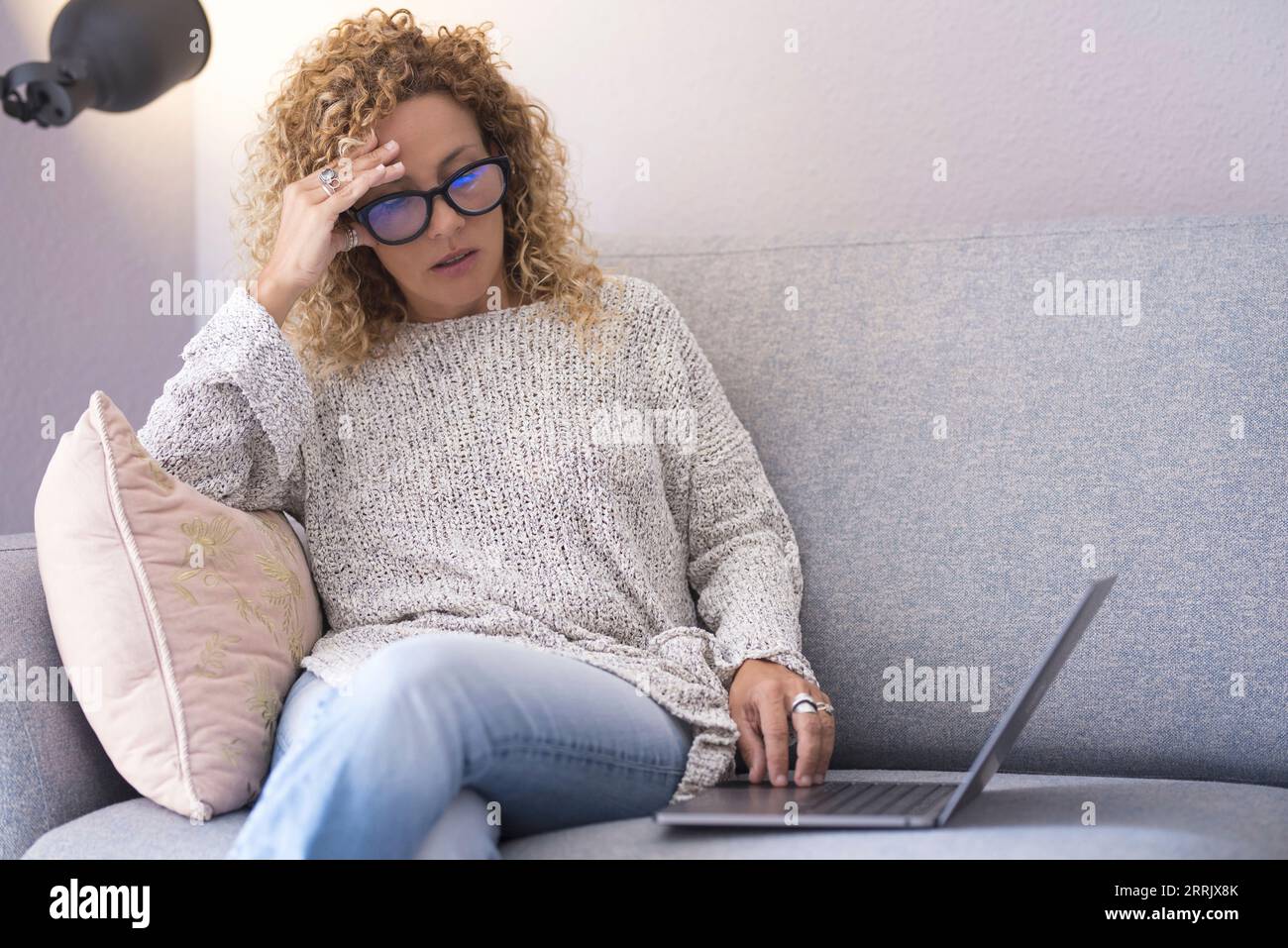 One woman at home using laptop on sofa with worried expression. Modern ...