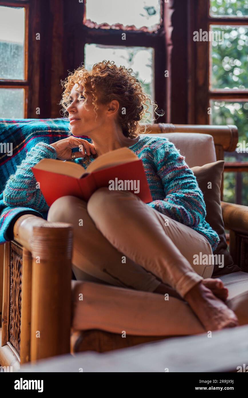 One alone adult woman at home spending time reading a book and looking outside. Indoor leisure ...