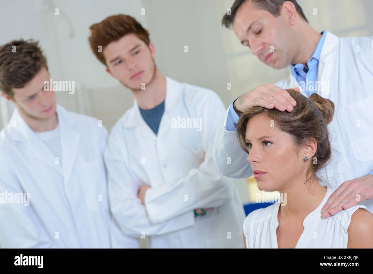 Students observing doctor with hand on patient's head and shoulder ...