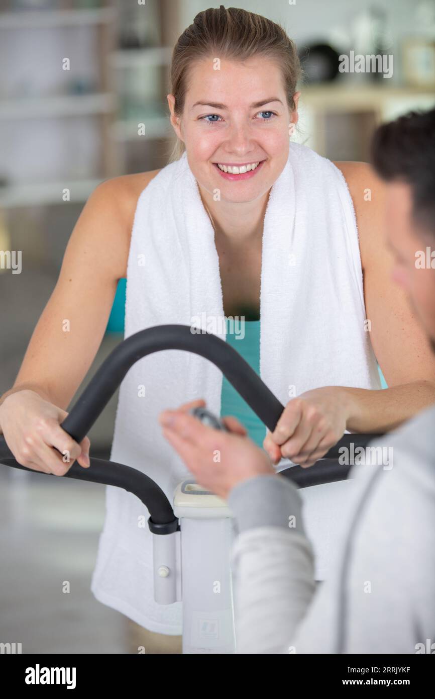 woman using an exercise machine while personal trainer holds stopwatch ...