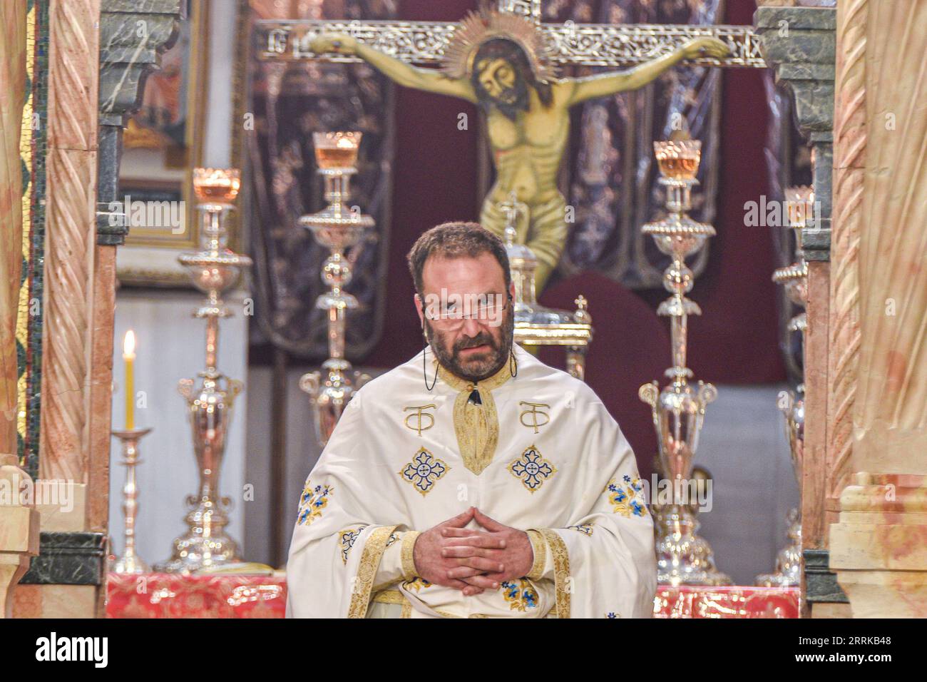 A middle-aged man wearing glasses is seated at an altar in a religious ...