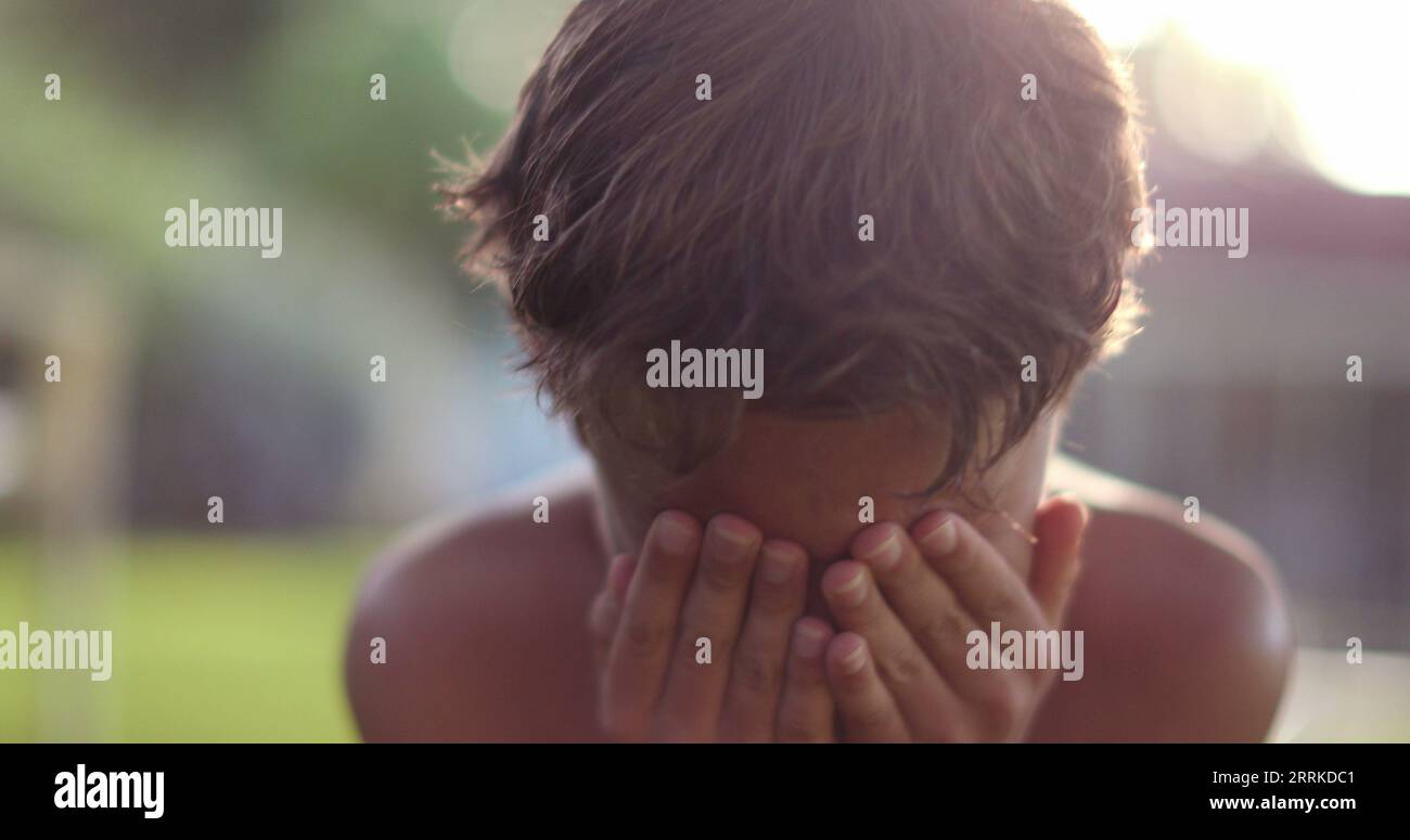 Boy covering face with hands feeling sad, child peeking from hands ...