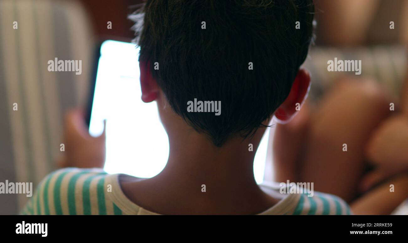 Back of child head staring at screen device at night Stock Photo - Alamy