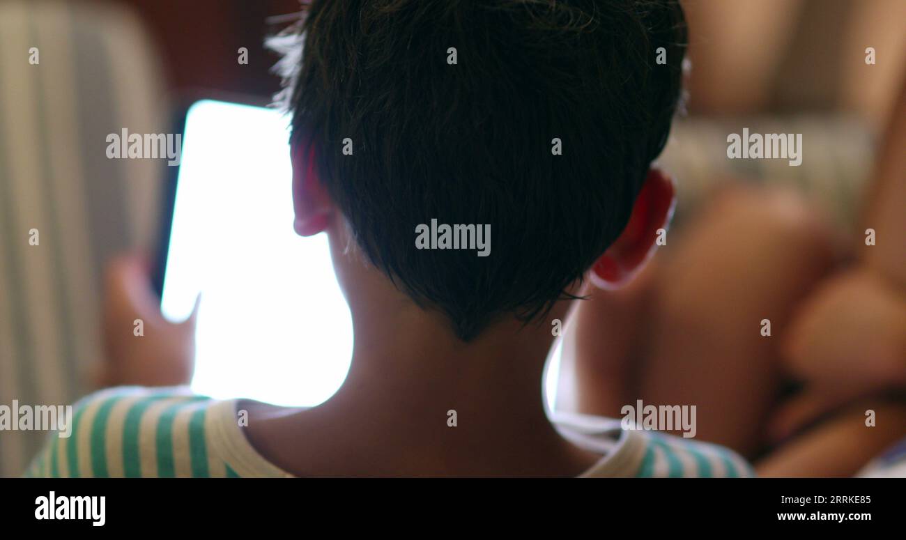 Back of child head staring at screen device at night Stock Photo - Alamy