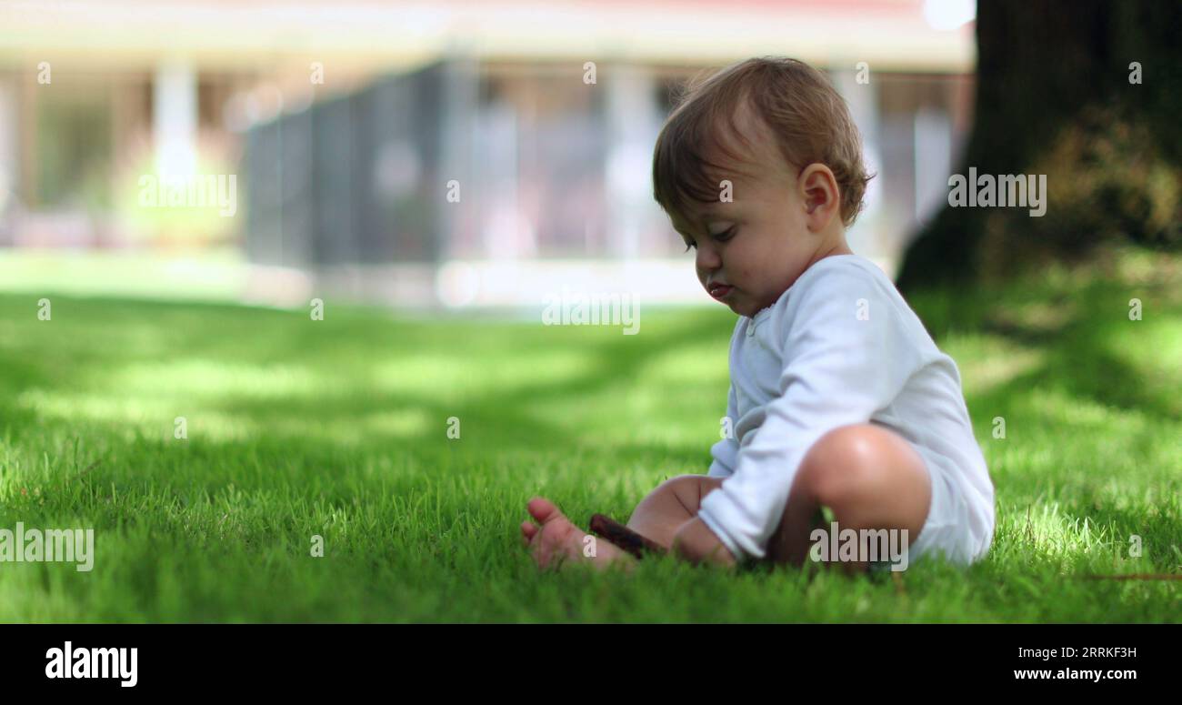 Adorable baby sitting outside in home lawn holding stick. Cute infant ...