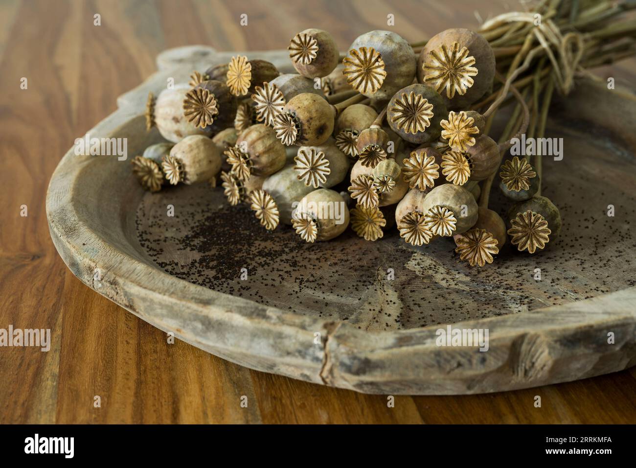 ripe poppy pods tied into a bouquet and seeds lie in an old wooden bowl ...