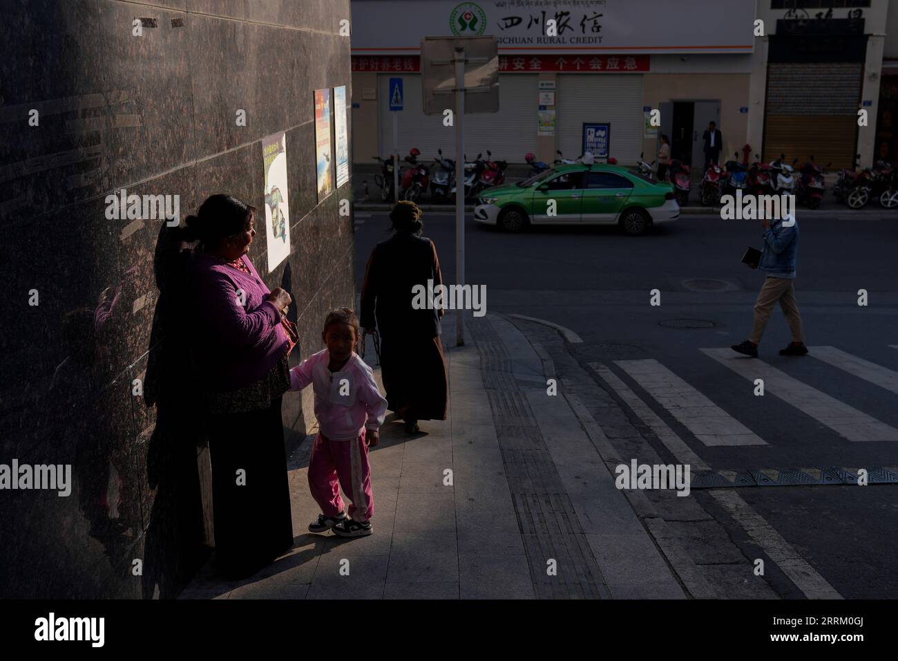 A Tibetan woman and a child stand in sunlight in Xiangcheng county ...