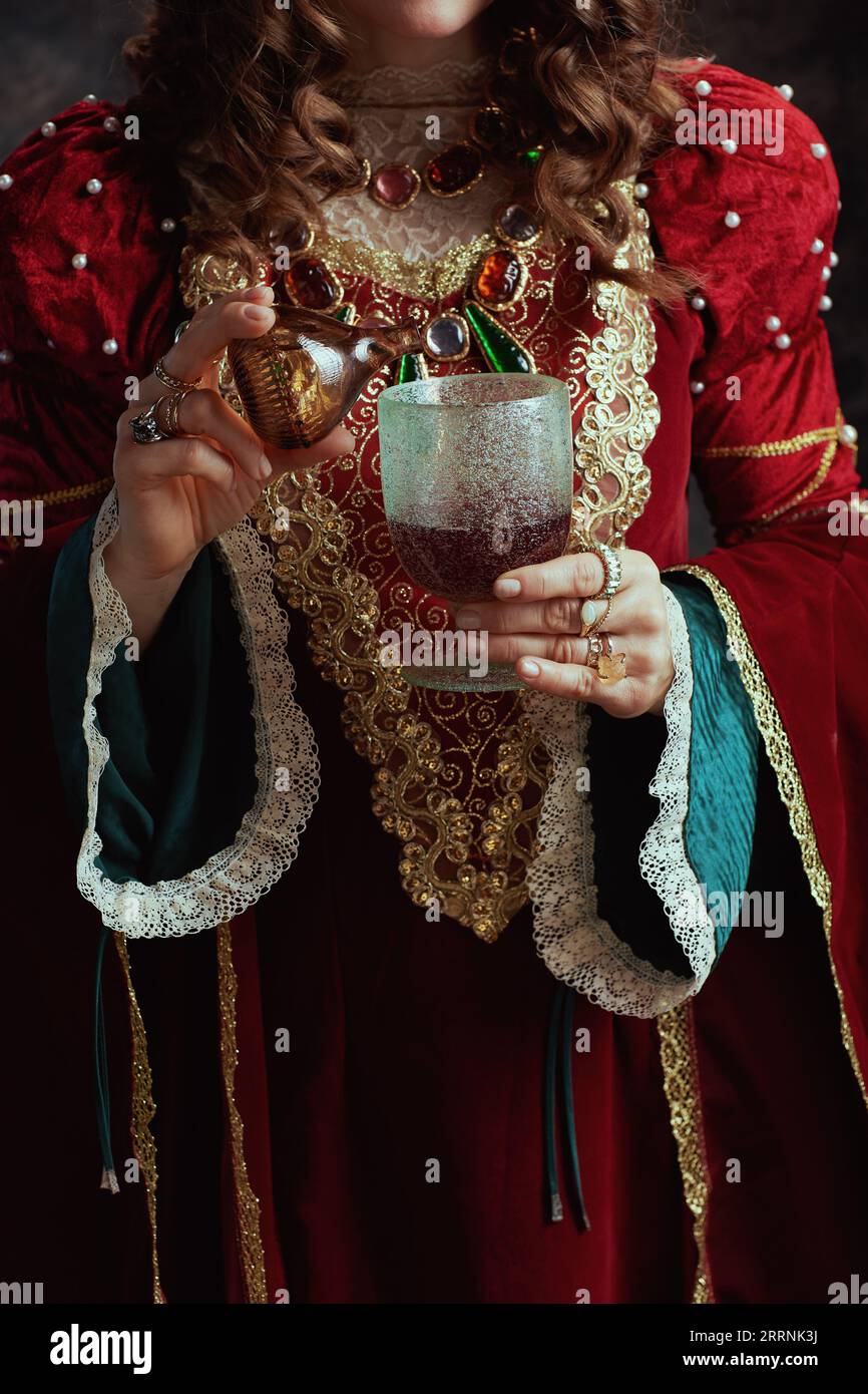 Closeup on medieval queen in red dress pouring poison into the goblet ...