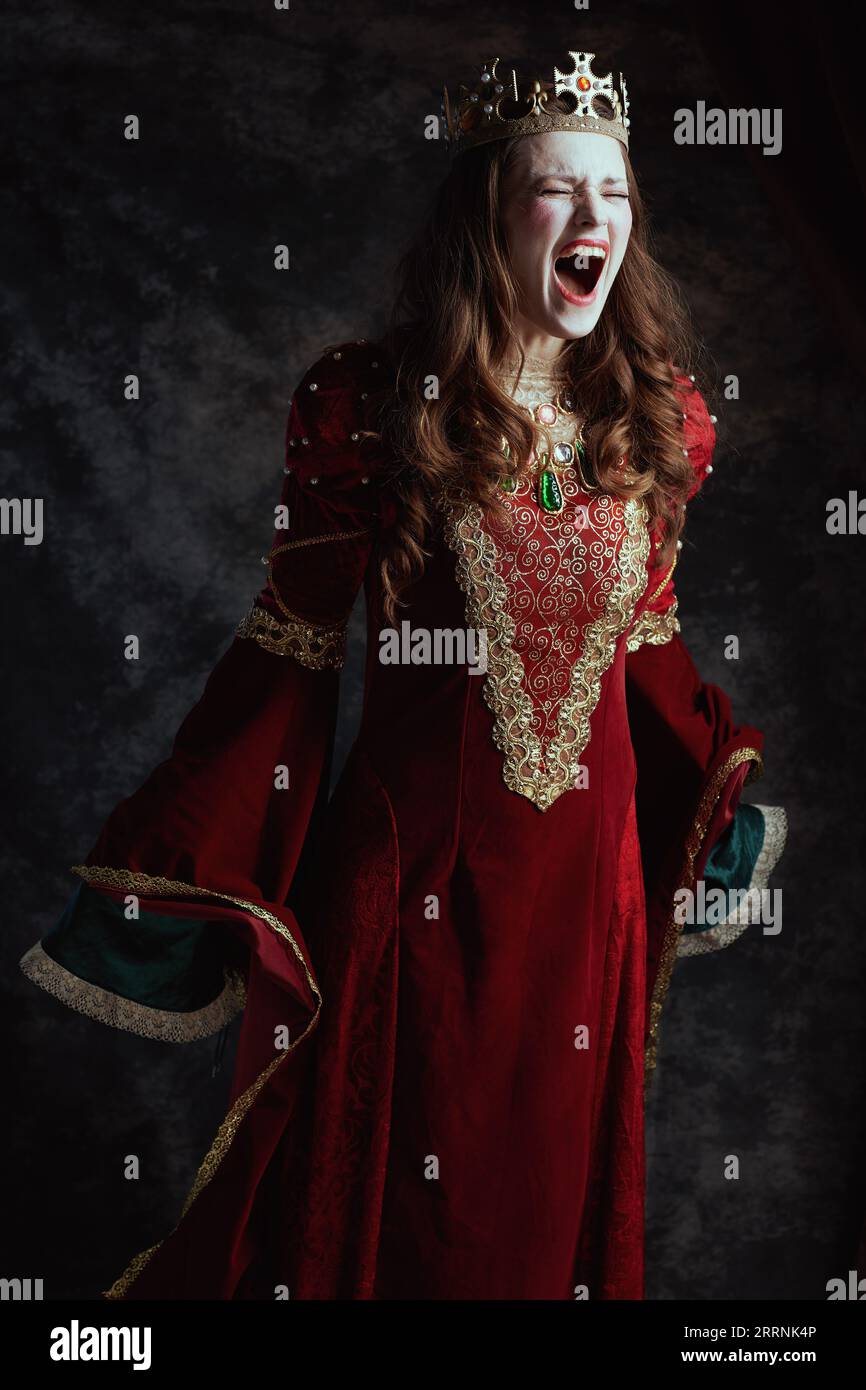 mad medieval queen in red dress with white makeup and crown on dark ...