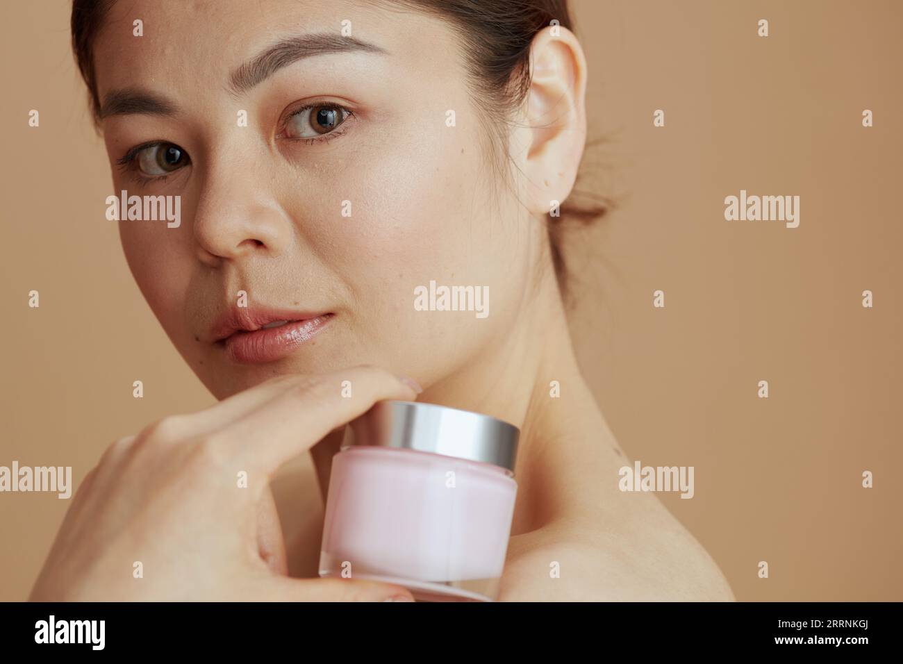 Portrait of modern woman with facial cream jar on beige background ...