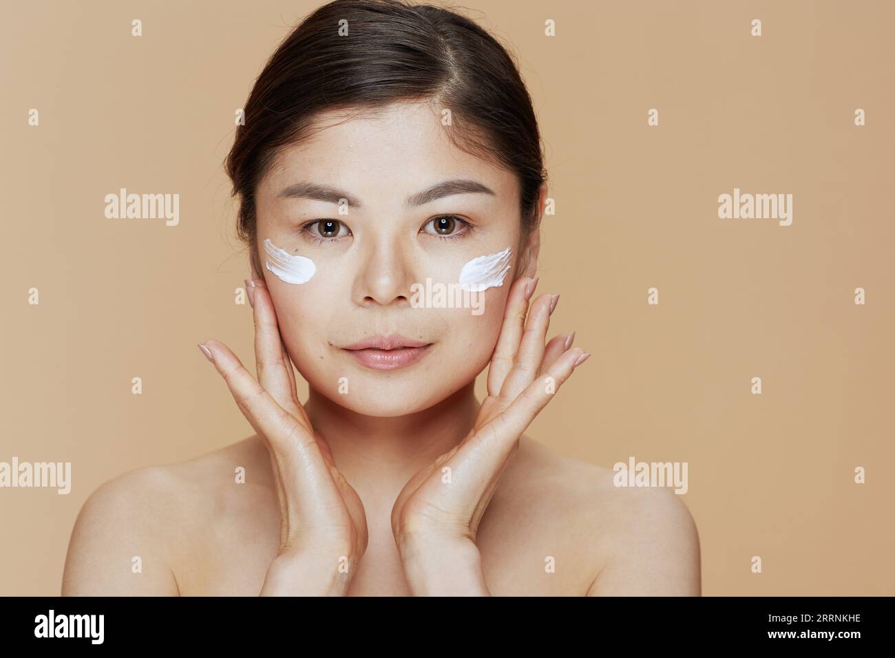 modern asian woman with facial cream on face isolated on beige ...