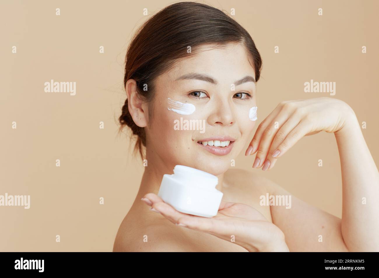 young asian female with facial cream jar and facial cream on face ...