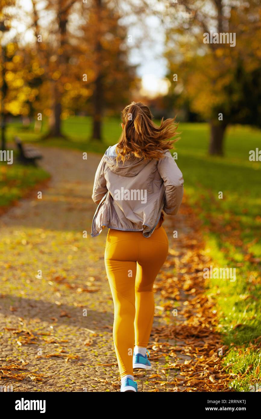 Hello autumn. Seen from behind woman in fitness clothes in the park ...