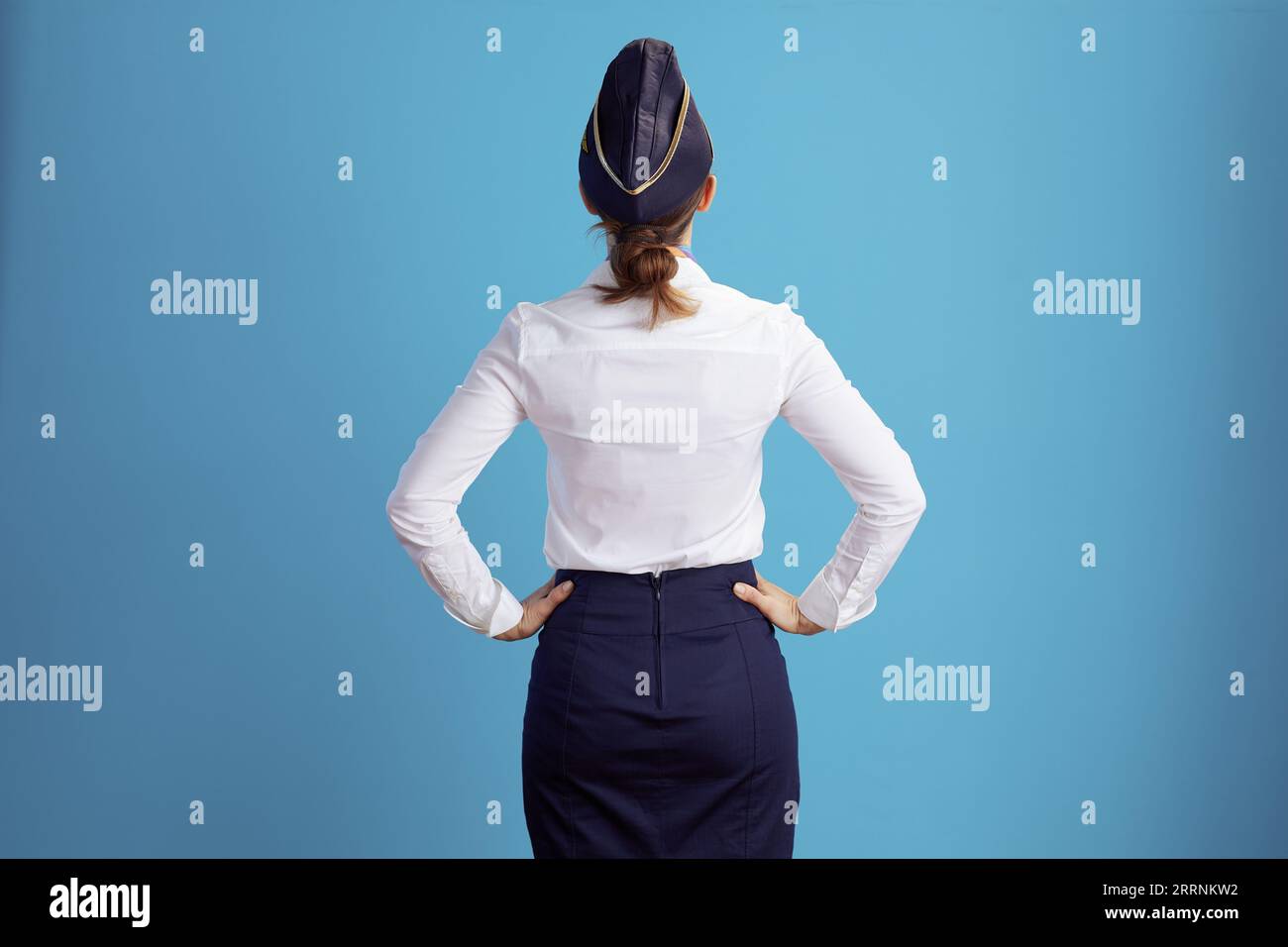 Seen from behind stylish female flight attendant against blue ...