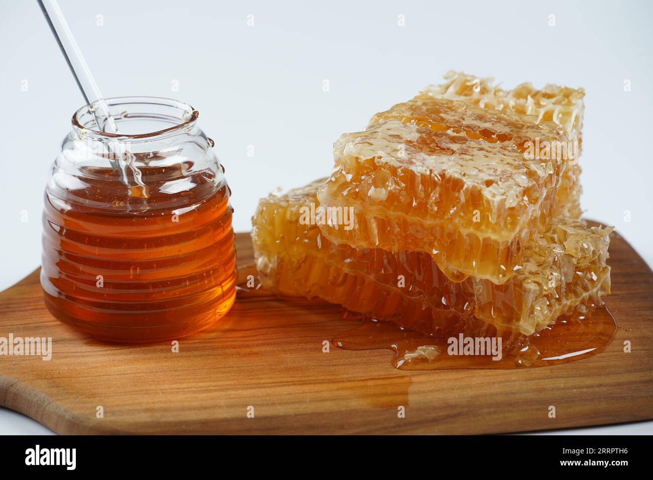 Honey jar and stick with liquid honey flowing on honeycomb pieces in a ...