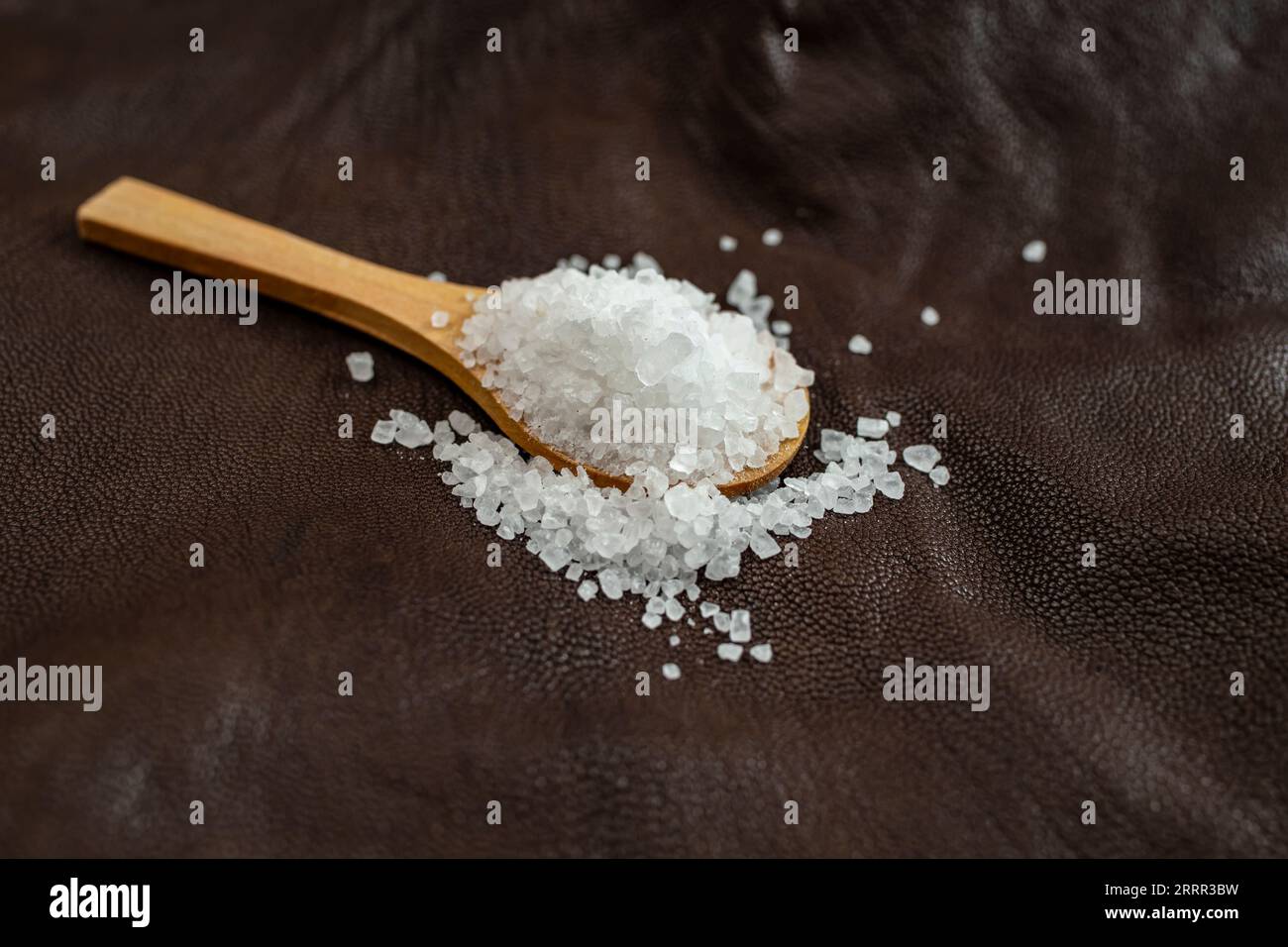 wooden teaspoon filled with white rock salt , on dark brown leather ...
