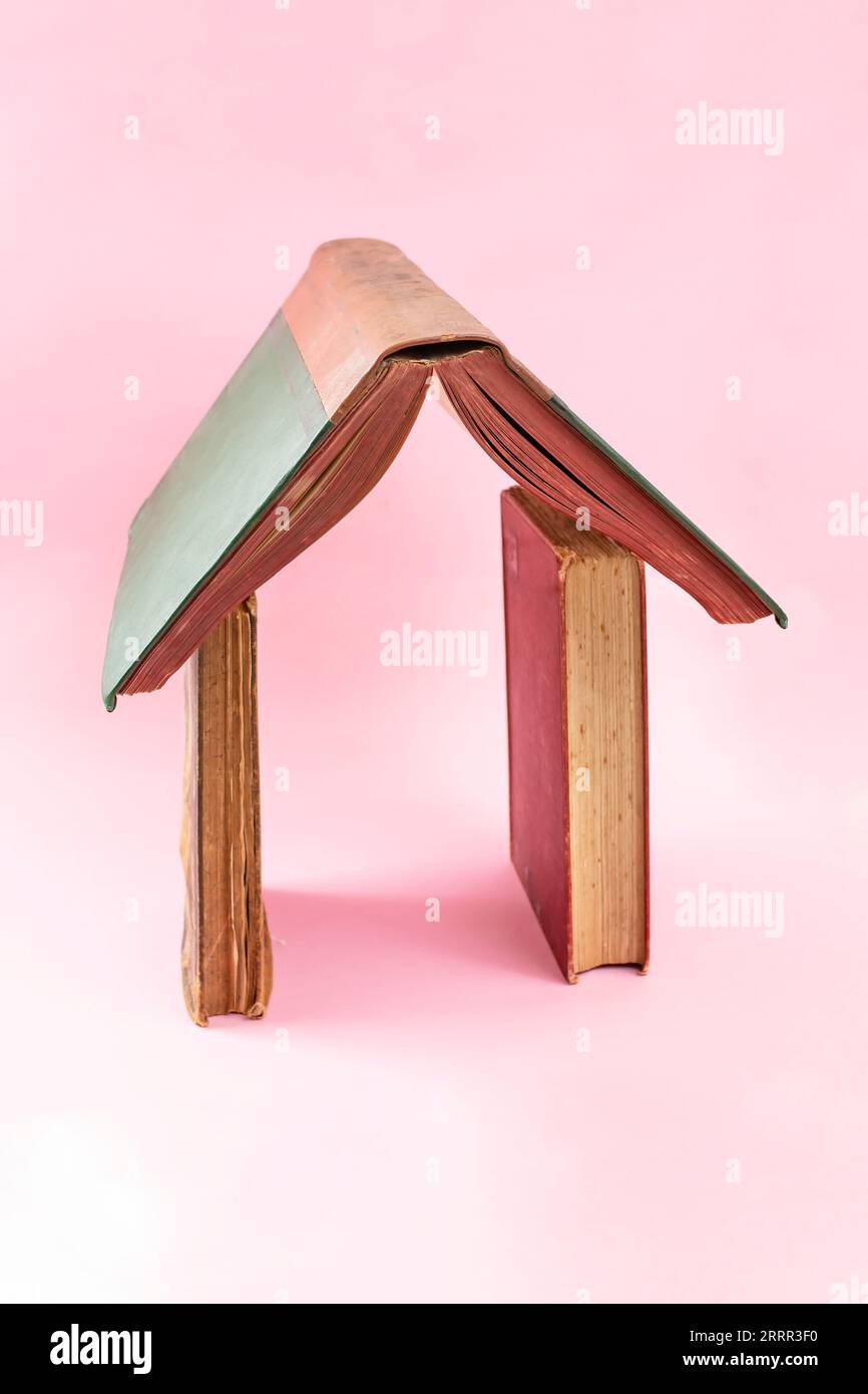 three vintage books arranged in the shape of a house on pink background ...