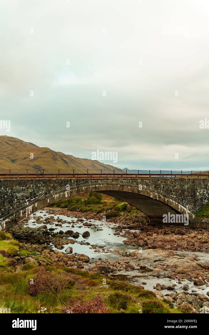 Stone bridge across dry river with rocky shore and mountain in the ...