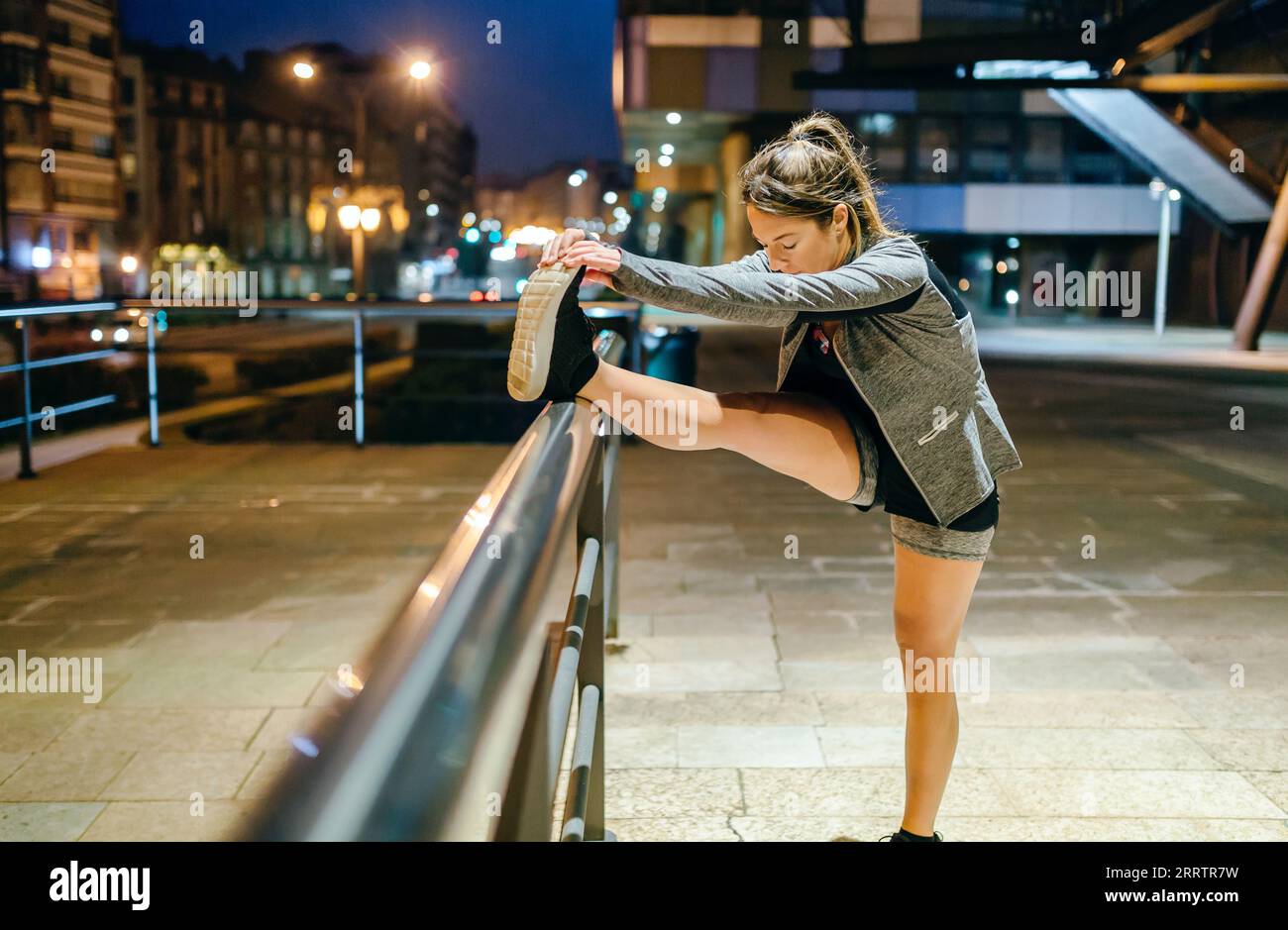 Young blonde woman runner with ponytail stretching her leg over a ...