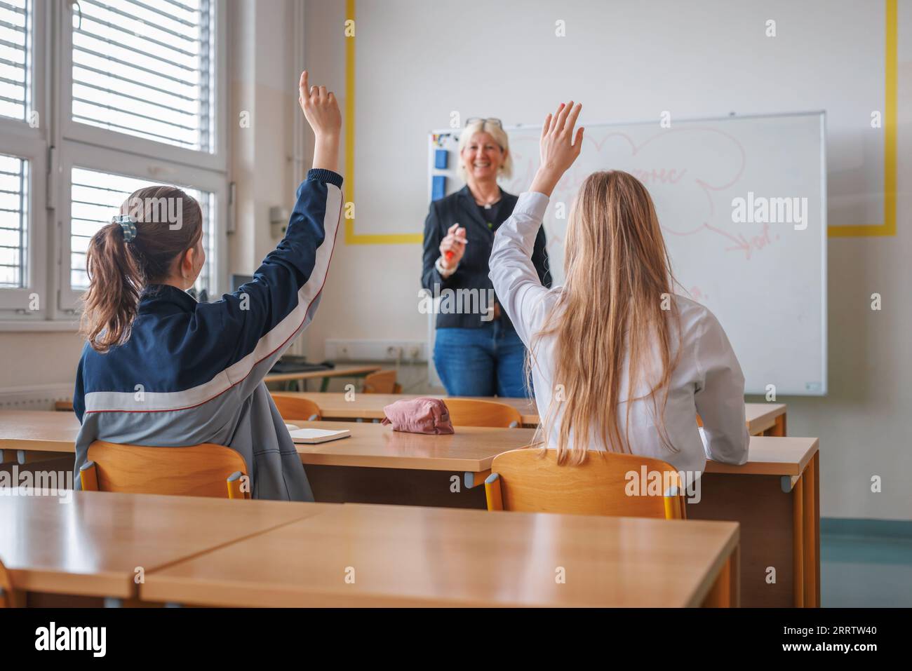 Girl student writes down notes and raises her hand while a female ...
