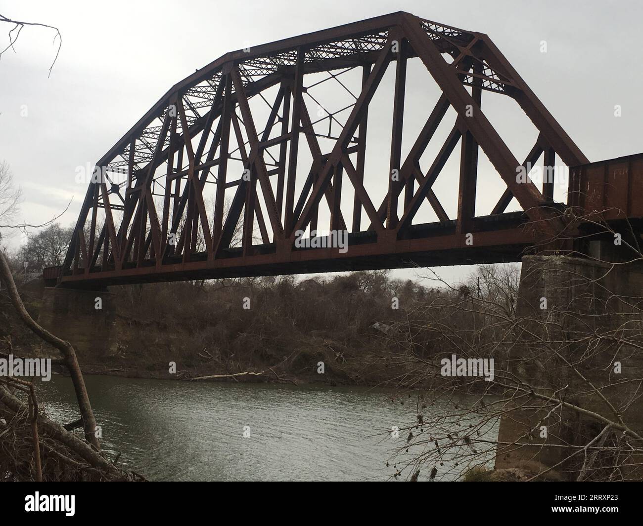 A rustic, metal railroad bridge spanning the width of a tranquil river ...