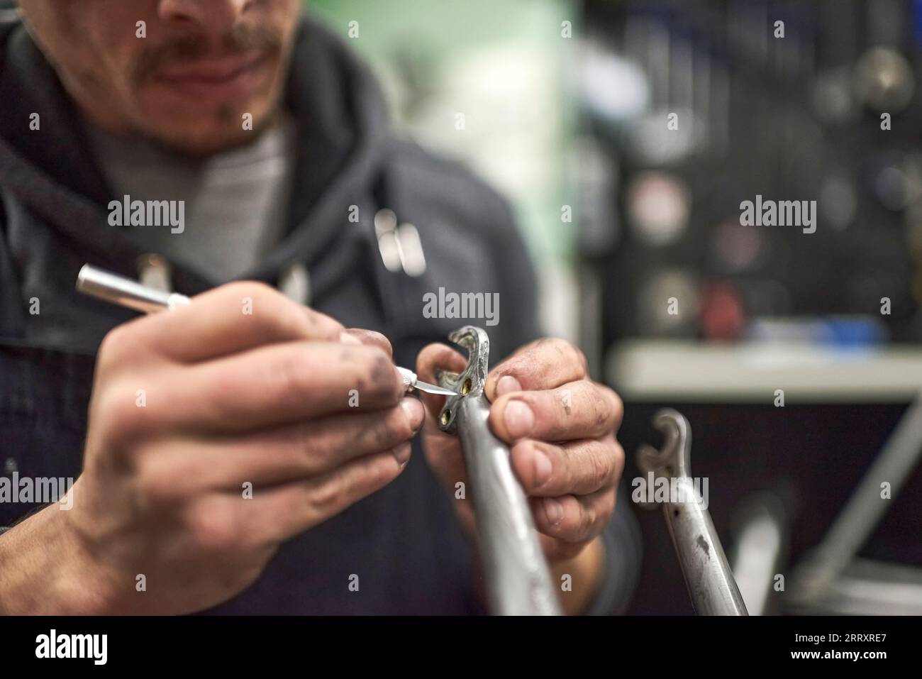 Hands of an hispanic man removing paint residue from a bicycle frame as ...