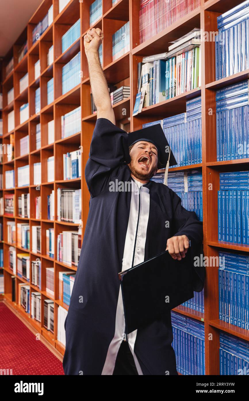 Young and thrilled graduate wearing his cap and gown celebrates getting ...