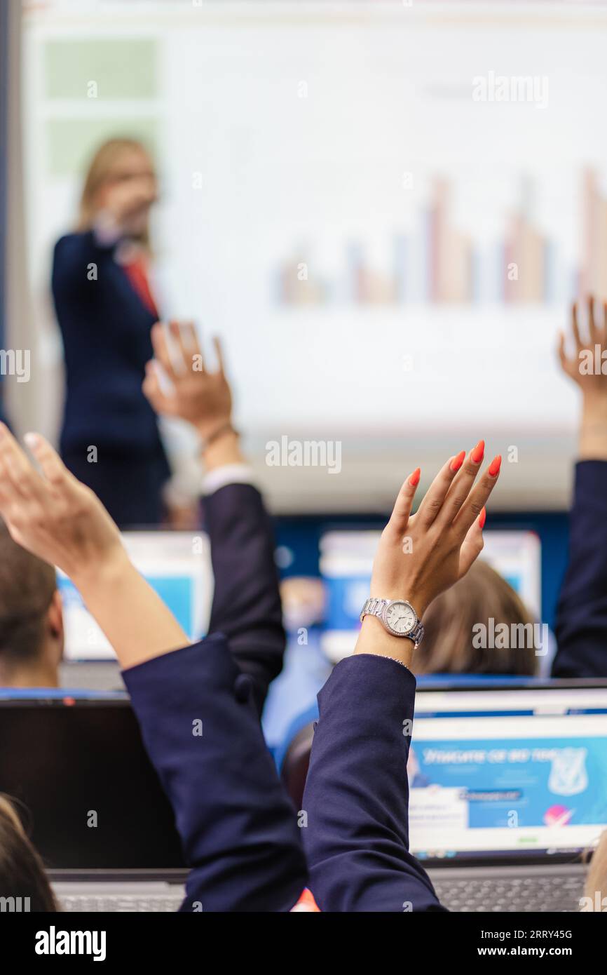 Students raising hands to answer or ask question while attending classes at modern classroom at ...