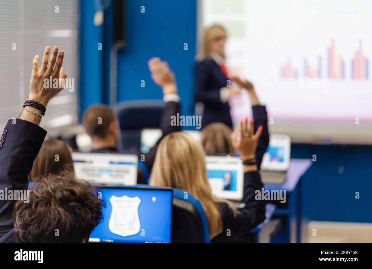Students raising hand while their professor is presenting and giving a ...