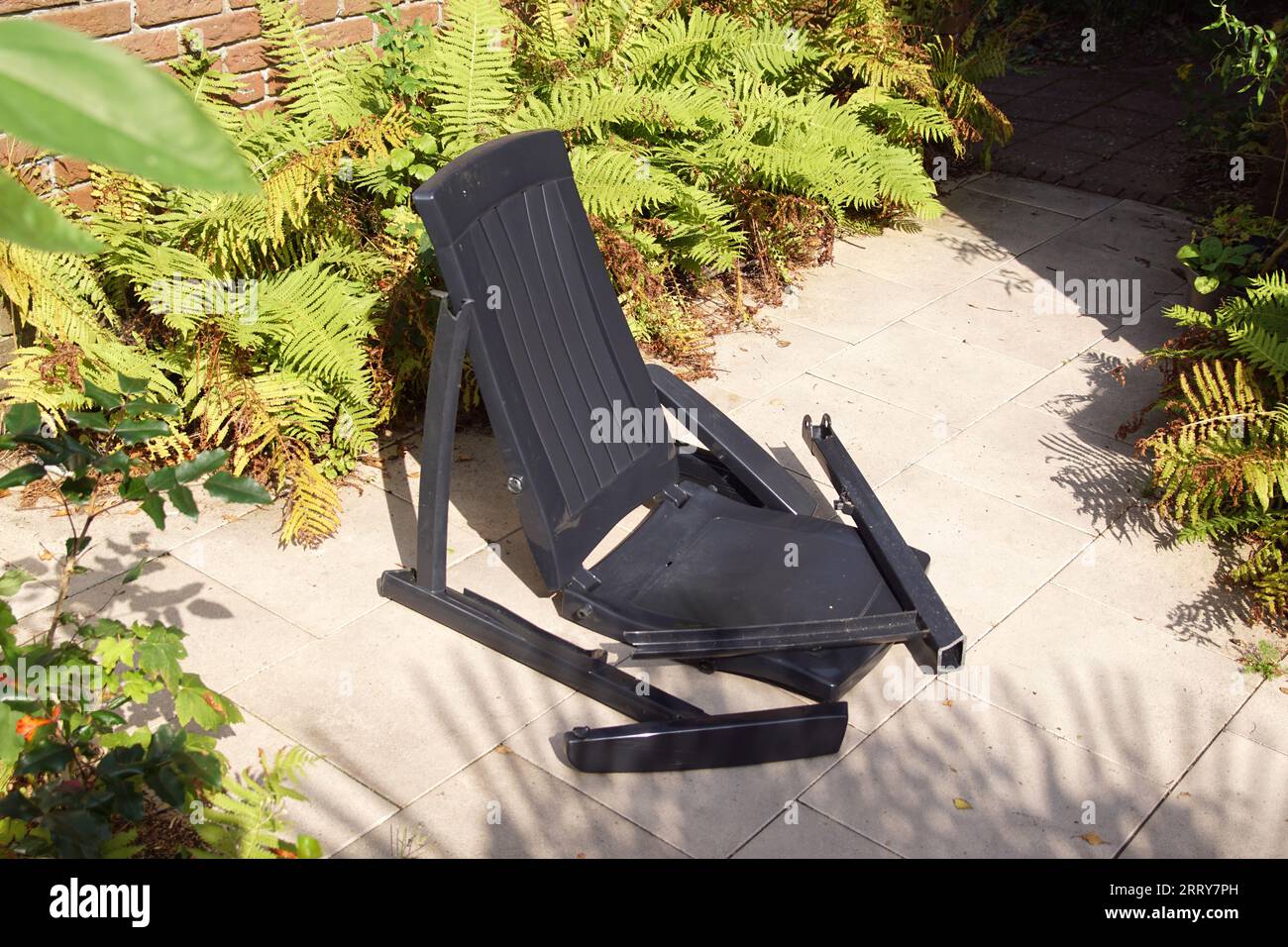Broken plastic black-gray garden chair. Collapsed. Dutch garden, summer ...